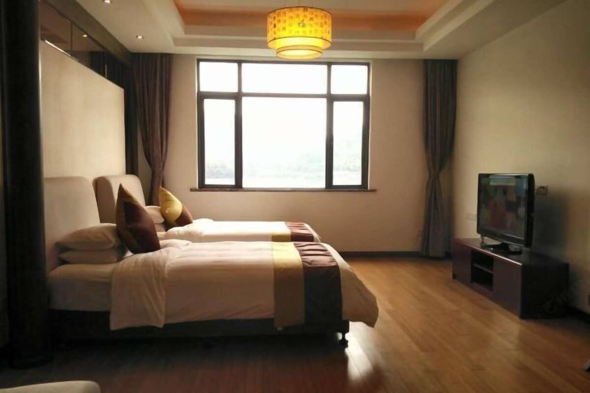 Quarto de hotel com cama, televisão, janela e uma lâmpada no teto.
