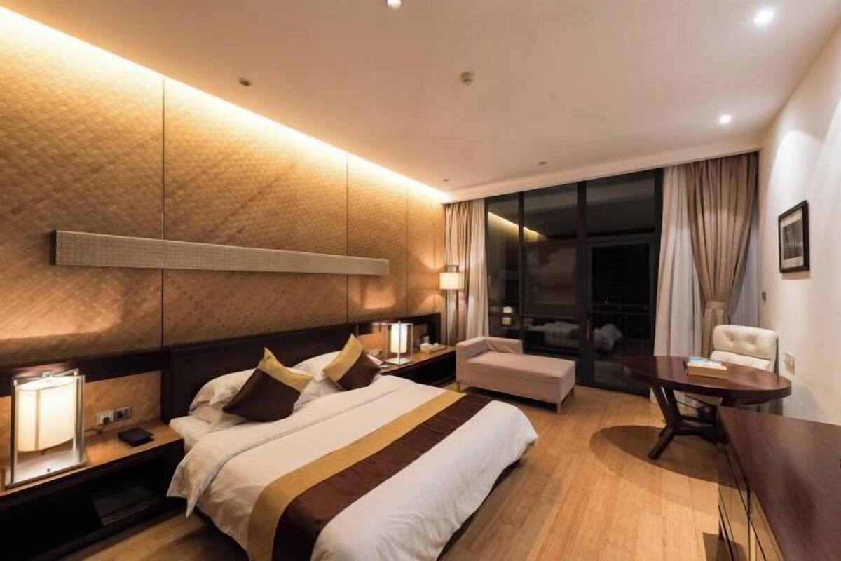 Quarto de hotel moderno com uma cama grande, mesas de cabeceira, uma escrivaninha e uma cadeira.