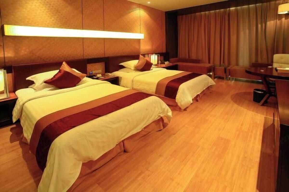 Quarto de hotel com duas camas, piso de madeira, uma escrivaninha e uma cadeira.