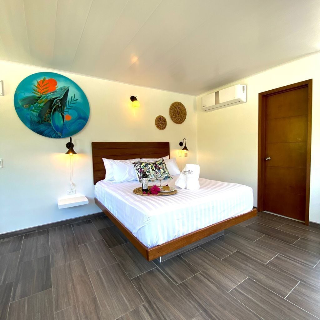 Quarto com cama de madeira, um ornamento redondo na parede, duas luminárias de parede e uma porta.