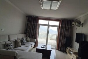 Uma sala de estar com sofá, mesa de centro, televisão e varanda com cortinas.