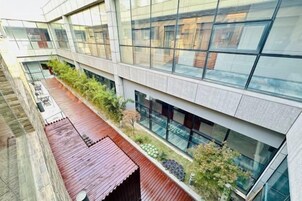 Um edifício moderno com fachada de vidro, deck de madeira e área ajardinada com plantas.