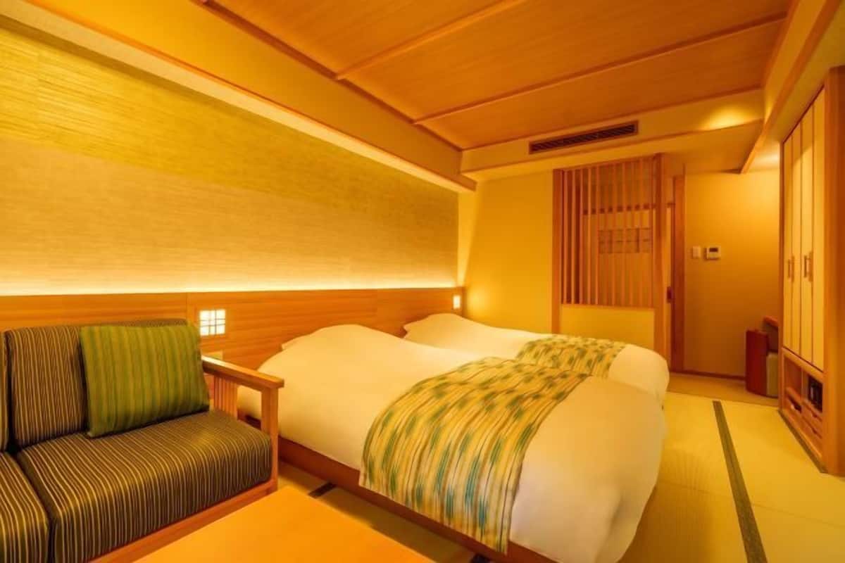 Quarto de hotel com cama, sofá, teto de madeira e porta deslizante.
