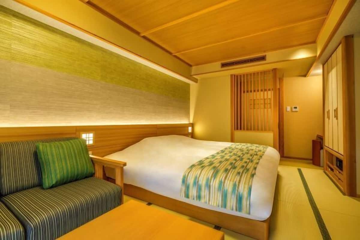 Um quarto japonês tradicional com tatames, uma cama de madeira baixa, um futon e portas deslizantes.
