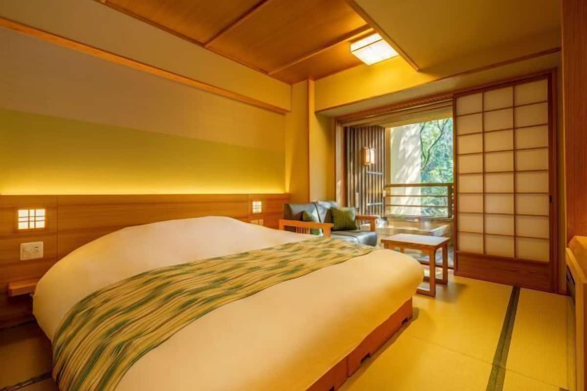 Um quarto em estilo japonês tradicional, com tatames, cama de madeira baixa, divisória deslizante shoji e vista para o verde lá fora.