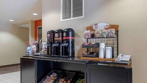 Estação de pequeno-almoço com serviço de buffet, máquinas de café, um telefone e uma variedade de alimentos embalados.