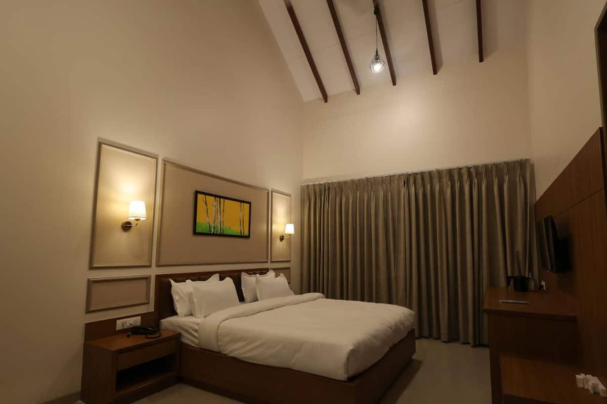 Quarto de hotel com cama, mesas de cabeceira, televisão e um quadro na parede.