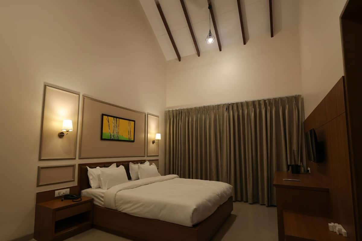 Quarto de hotel com uma cama grande, mesa de cabeceira, televisão e um quadro na parede.