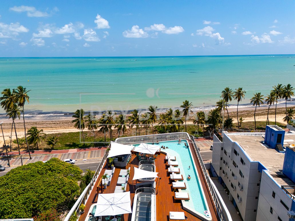 Convés de navio de cruzeiro com piscina, espreguiçadeiras e vista para o mar e a praia.