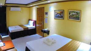 Quarto de hotel com duas camas de solteiro, uma escrivaninha com cadeira, uma mesinha com garrafa e copos, e telefone fixo na parede.