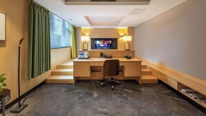 Quarto de hotel com secretária, televisão e duas luminárias.
