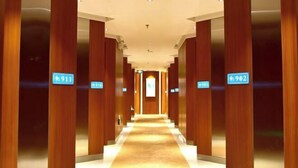 Corredor de hotel com painéis de madeira e piso coberto por carpete. Placas indicam os números dos quartos 911 e 902.