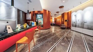 Um saguão moderno de hotel com balcão de recepção, área de estar e uma tela digital grande.
