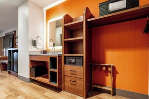 Quarto de hotel compacto com toucador de madeira, televisão integrada e pequena cozinha.