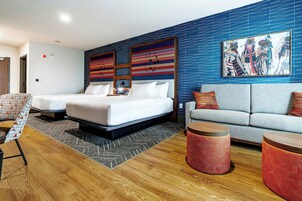 Quarto de hotel moderno com uma cama grande, um sofá, duas mesinhas de cabeceira e uma parede com padrão.