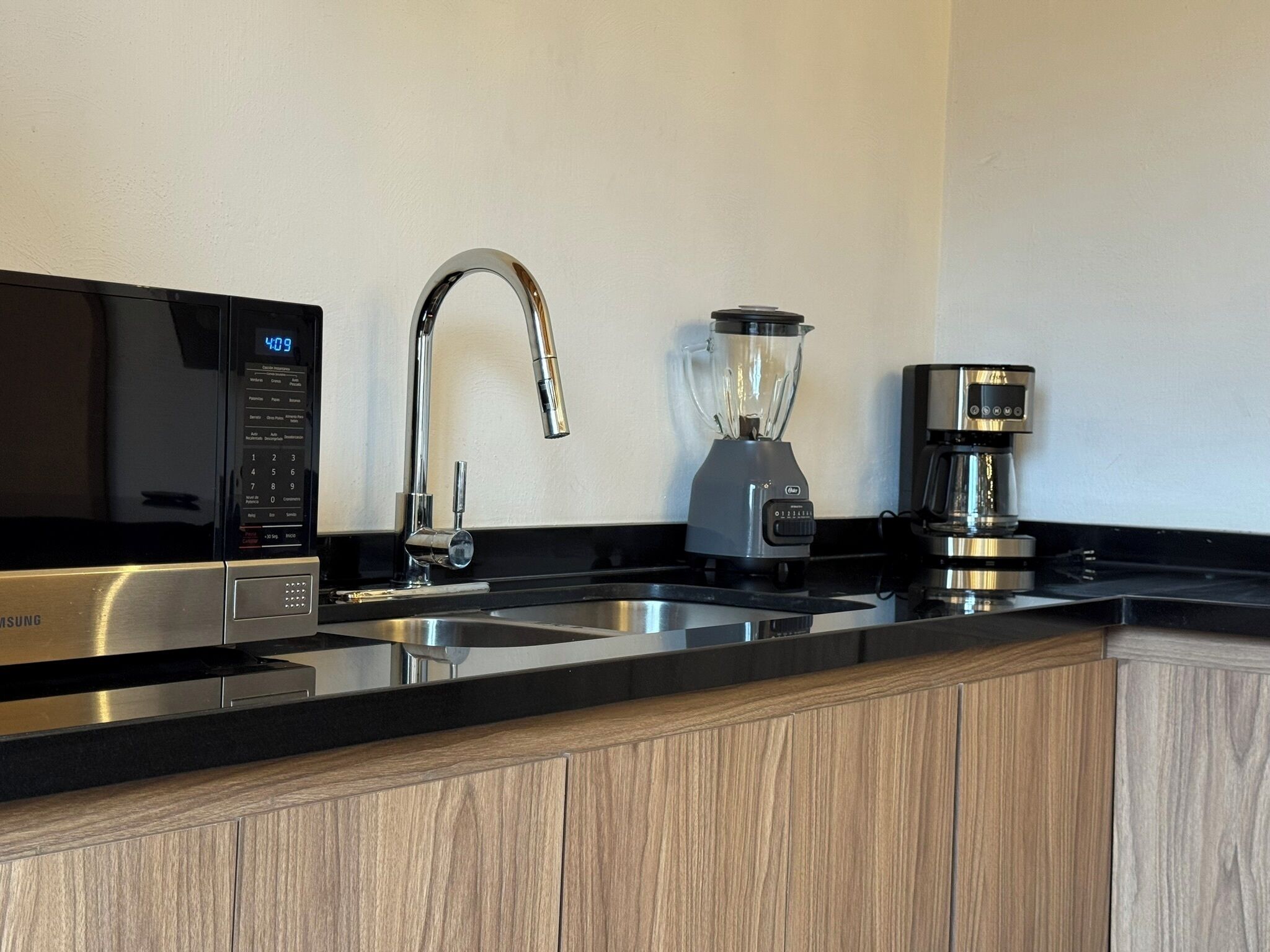 Uma cozinha moderna com eletrodomésticos de aço inoxidável, incluindo um micro-ondas, um liquidificador e uma cafeteira.