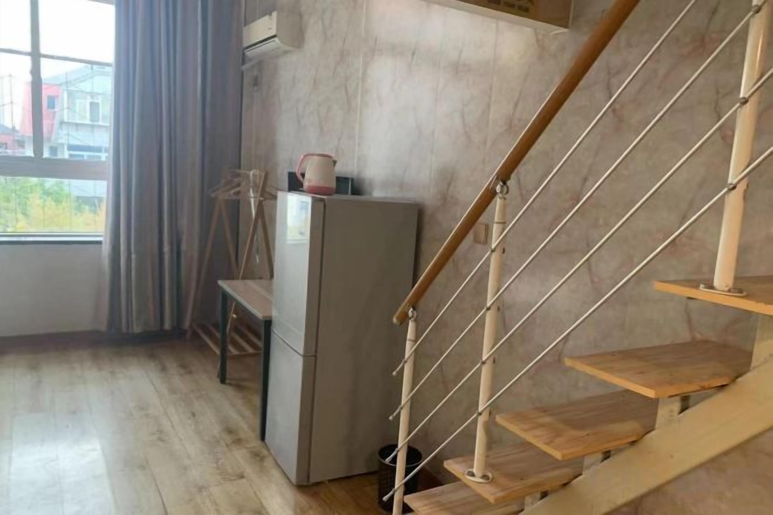 Quarto com escada de madeira, geladeira e janela com cortinas.