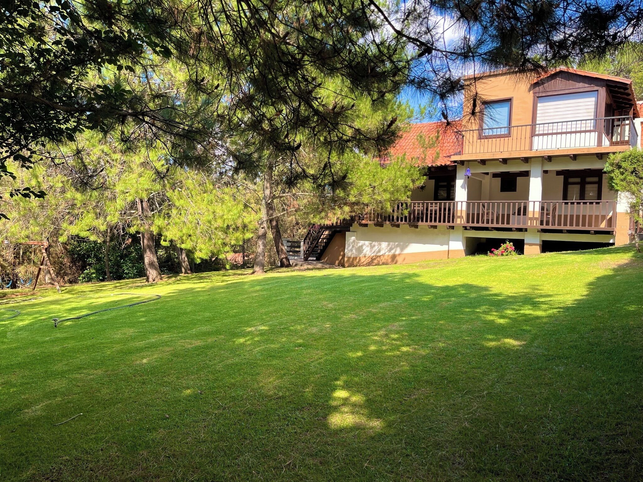 Uma casa de dois andares com varanda, cercada por um gramado bem cuidado e árvores.