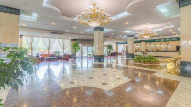 Um hall amplo com piso de mármore polido, grandes lustres e áreas de estar.