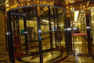 Porta giratória com painéis de vidro e piso de mármore.