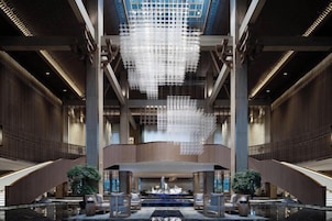 Um hall amplo com um grande candelabro, uma fonte central e uma escadaria para os andares superiores.