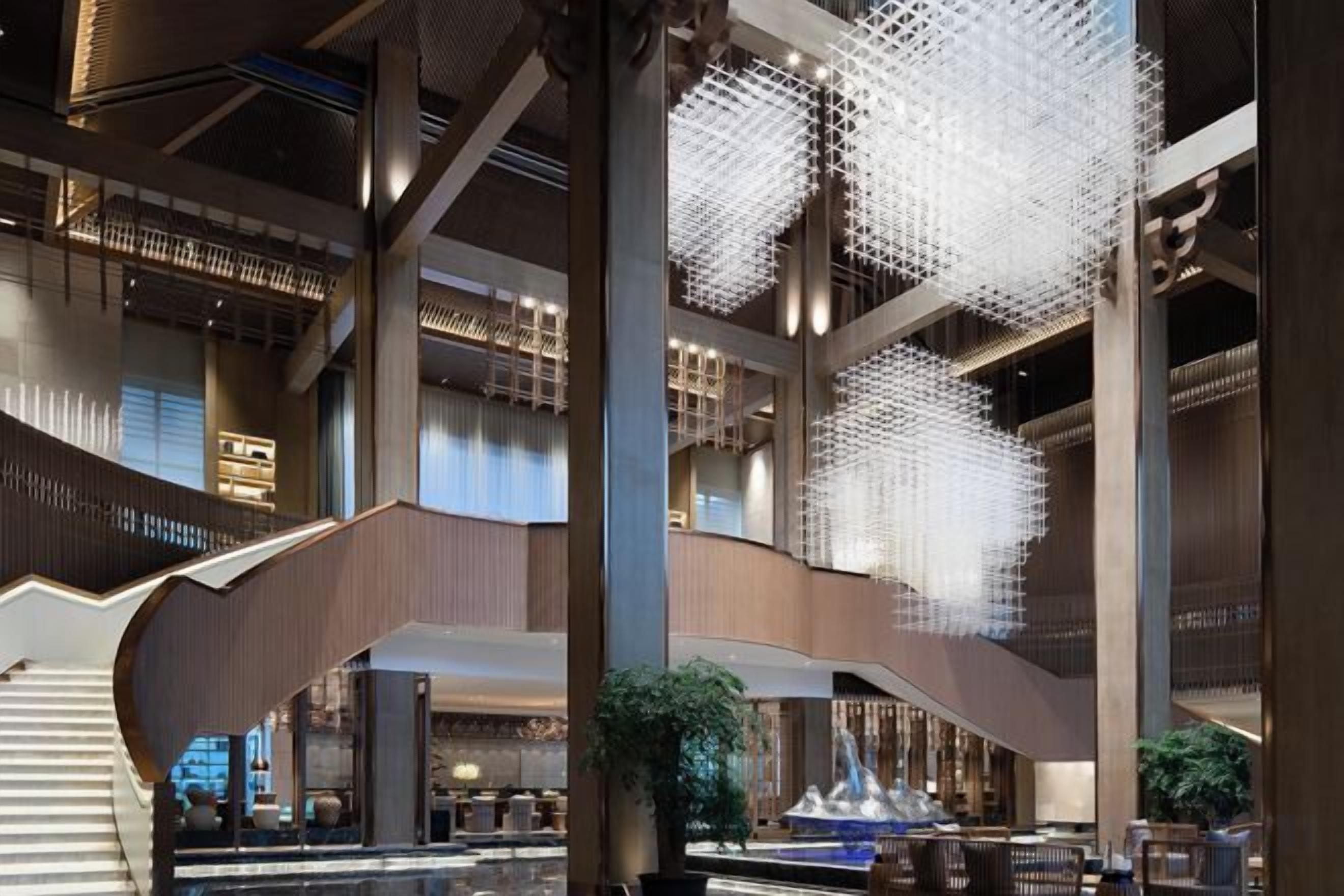 Um hall espaçoso com uma escadaria imponente, um elemento decorativo de água e um lustre moderno.