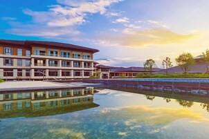 Um edifício moderno com uma piscina refletora na frente, cercado por vegetação e céu claro.