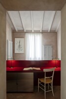 Sala de estudos com escrivaninha, cadeira, livros e janela com cortinas.