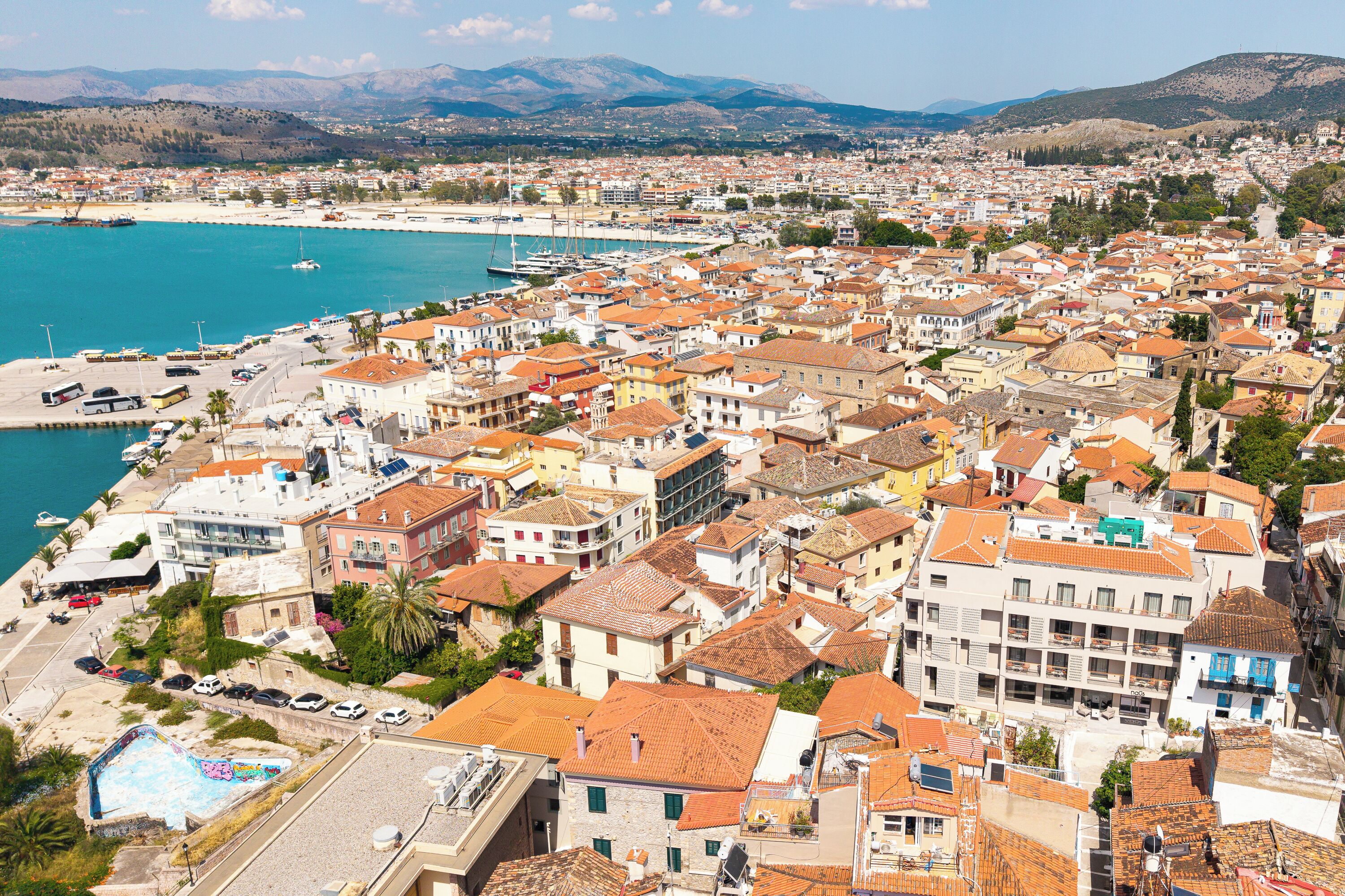 Uma vila costeira com um porto de iates, edifícios em socalcos e uma praia.