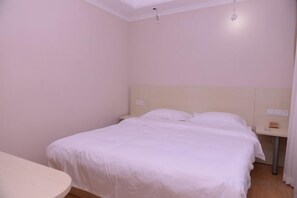 Quarto de hotel padrão com uma cama de solteiro, mesa de cabeceira e pequena escrivaninha.