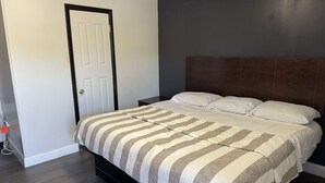 Quarto com cama, cabeceira escura, porta e mesa de cabeceira.