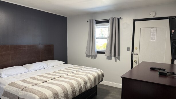 Quarto de hotel com cama, escrivaninha, janela com cortinas e porta.