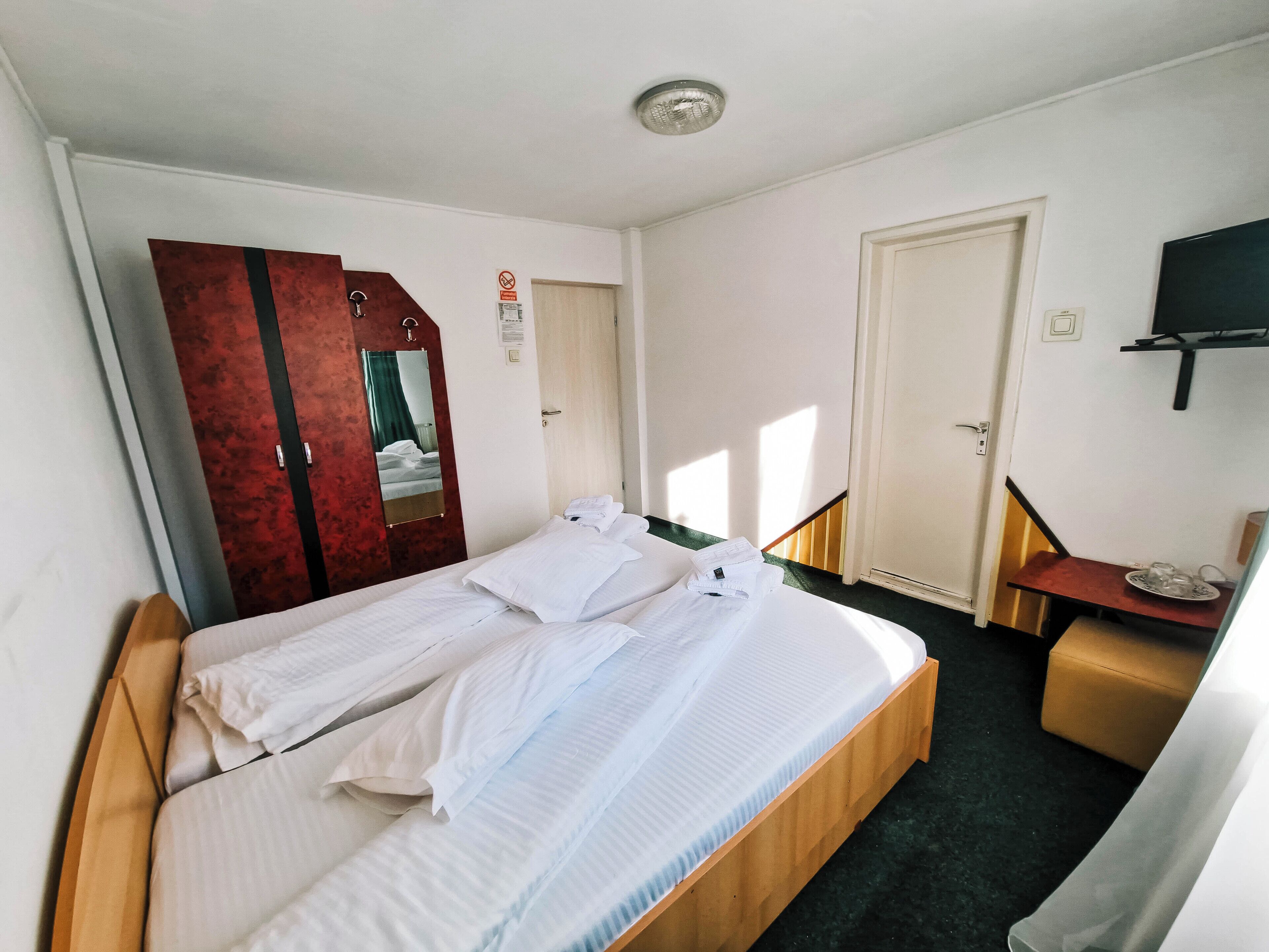 Quarto de hotel com uma cama, espelho, televisão e uma pequena mesa.