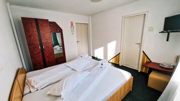 Quarto de hotel com uma cama, espelho, televisão e uma pequena mesa.