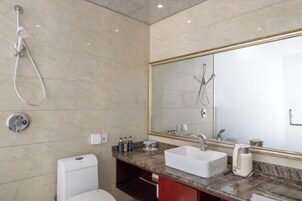 Casa de banho moderna com soalho em mármore, um espelho grande, lavatório branco e chuveiro manual.