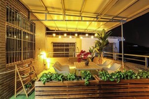 Uma área externa com mesas e cadeiras, cercada por plantas e um corrimão.