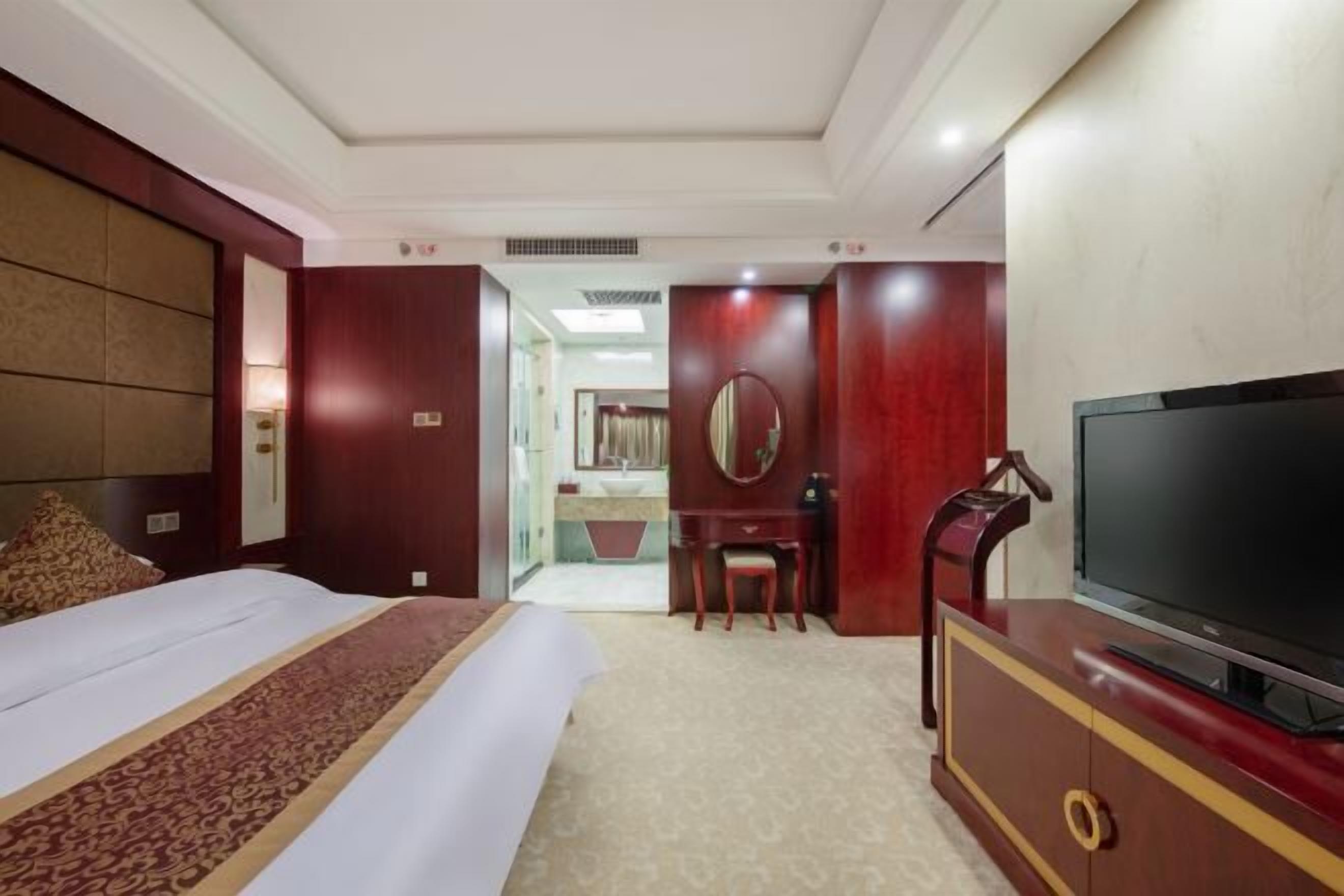 Quarto de hotel com cama, televisão, escrivaninha e espelho.