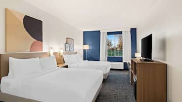 Quarto de hotel com duas camas, uma escrivaninha, televisão e janela com cortinas.