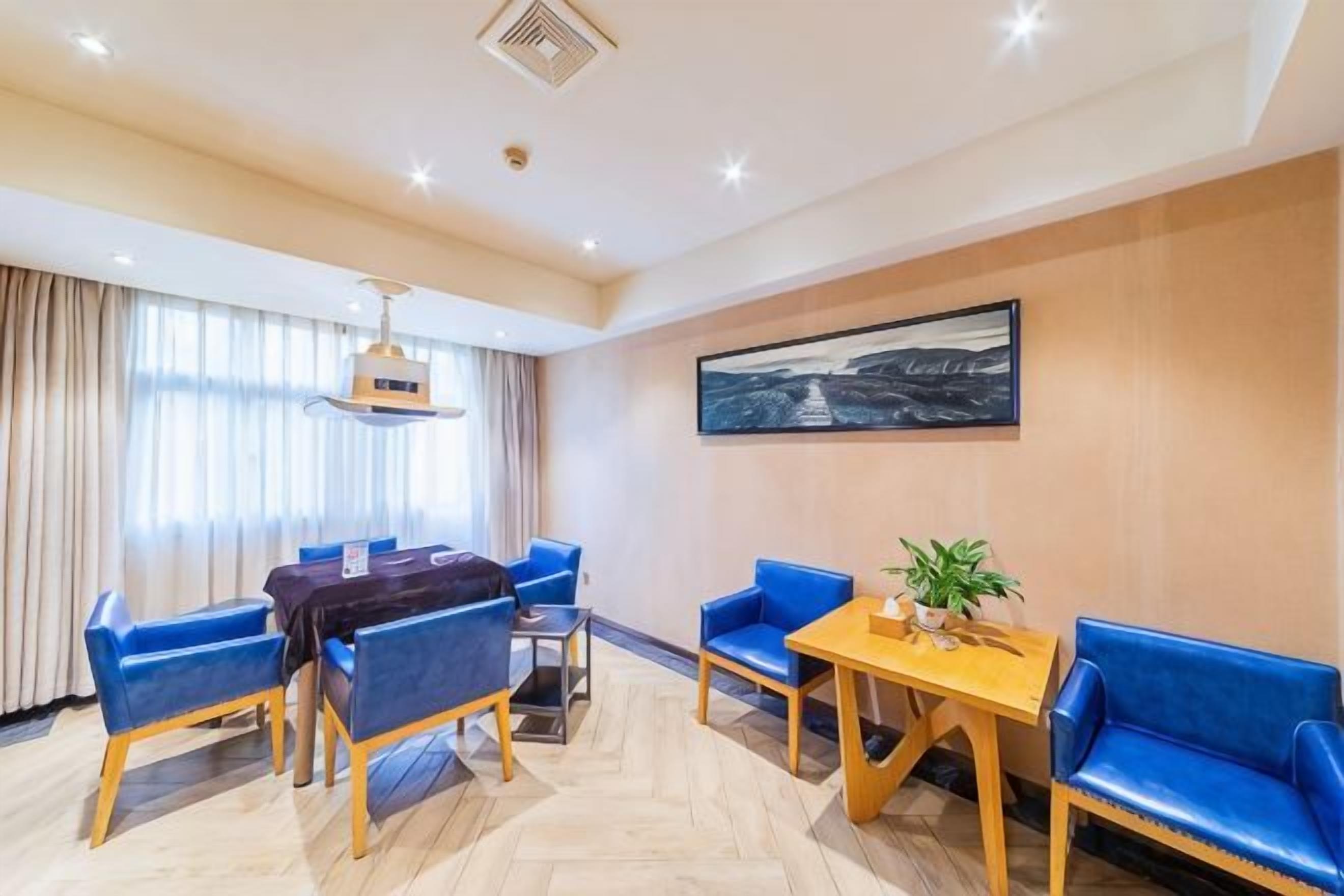 Quarto de hotel com área de jantar, conjunto de sofás, mesa com planta e um quadro na parede.