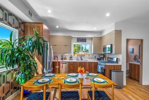 Uma cozinha moderna com armários de madeira, uma área de jantar com mesa de madeira posta para quatro pessoas e uma janela grande que oferece iluminação natural.