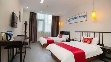 Quarto de hotel com duas camas, uma escrivaninha, uma cadeira, uma televisão e uma janela com cortinas.
