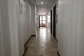 Um corredor com piso de azulejos, portas em ambos os lados e luminária no teto.