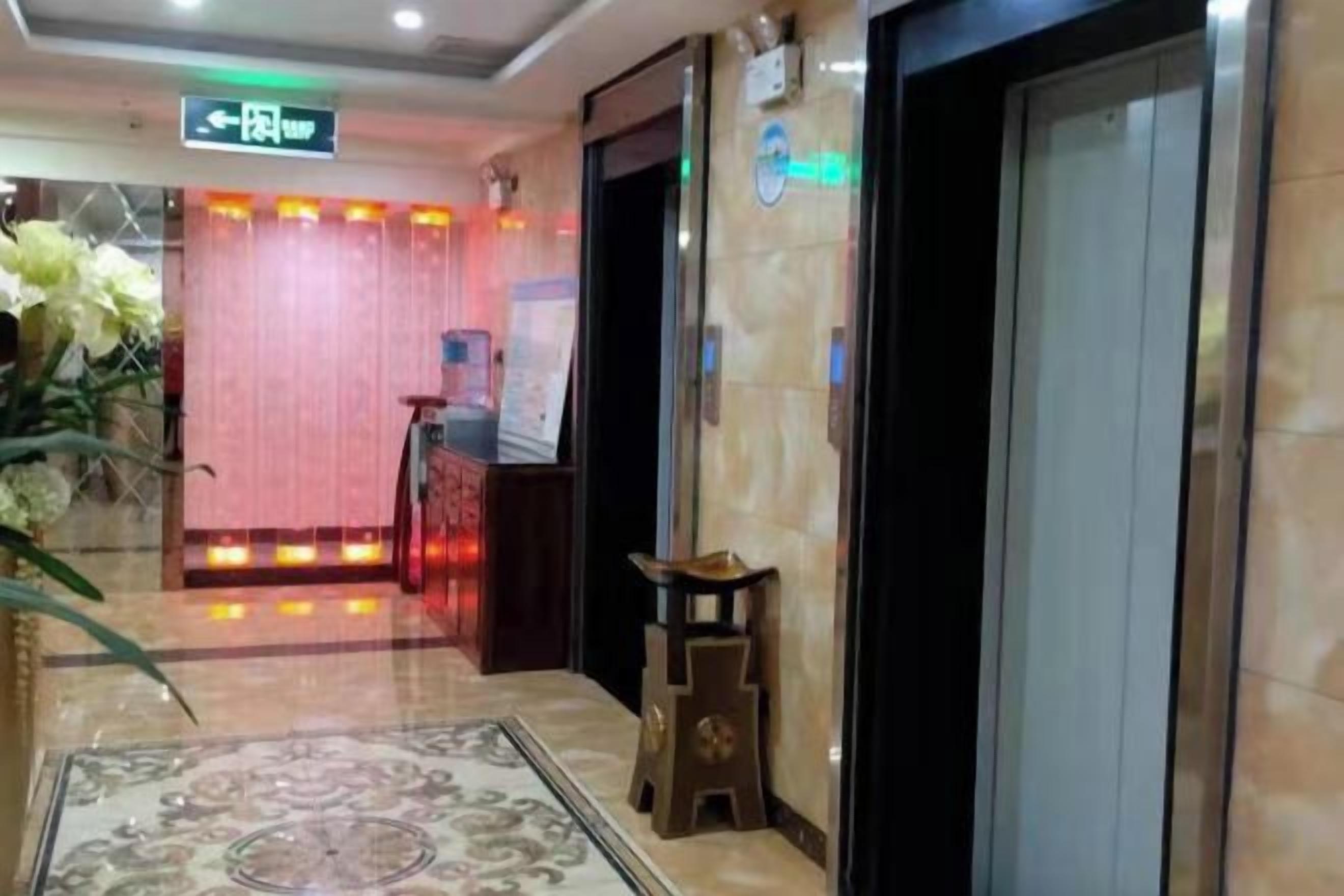 Uma área de recepção de hotel, com balcão, um banquinho pequeno e piso de azulejos.