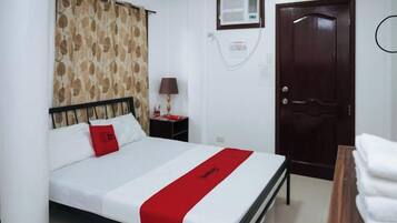 Quarto de hotel com cama, mesa de cabeceira, abajur, porta e janela.