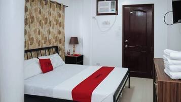 Quarto de hotel com uma cama, mesa de cabeceira, abajur, porta e ar condicionado fixado na parede.