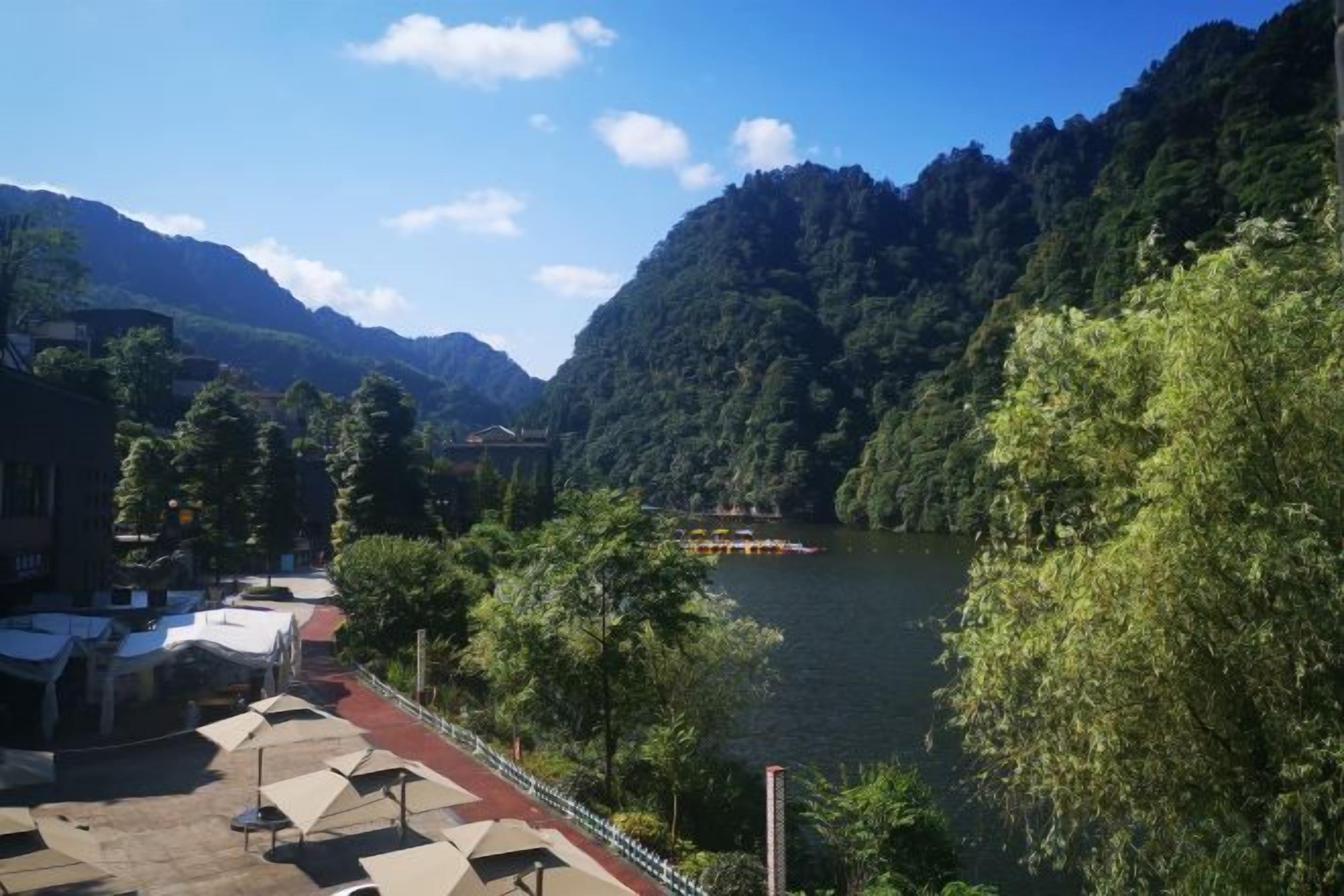 Vista para o rio, com calçada à beira da água, árvores e um edifício com mesas ao ar livre.