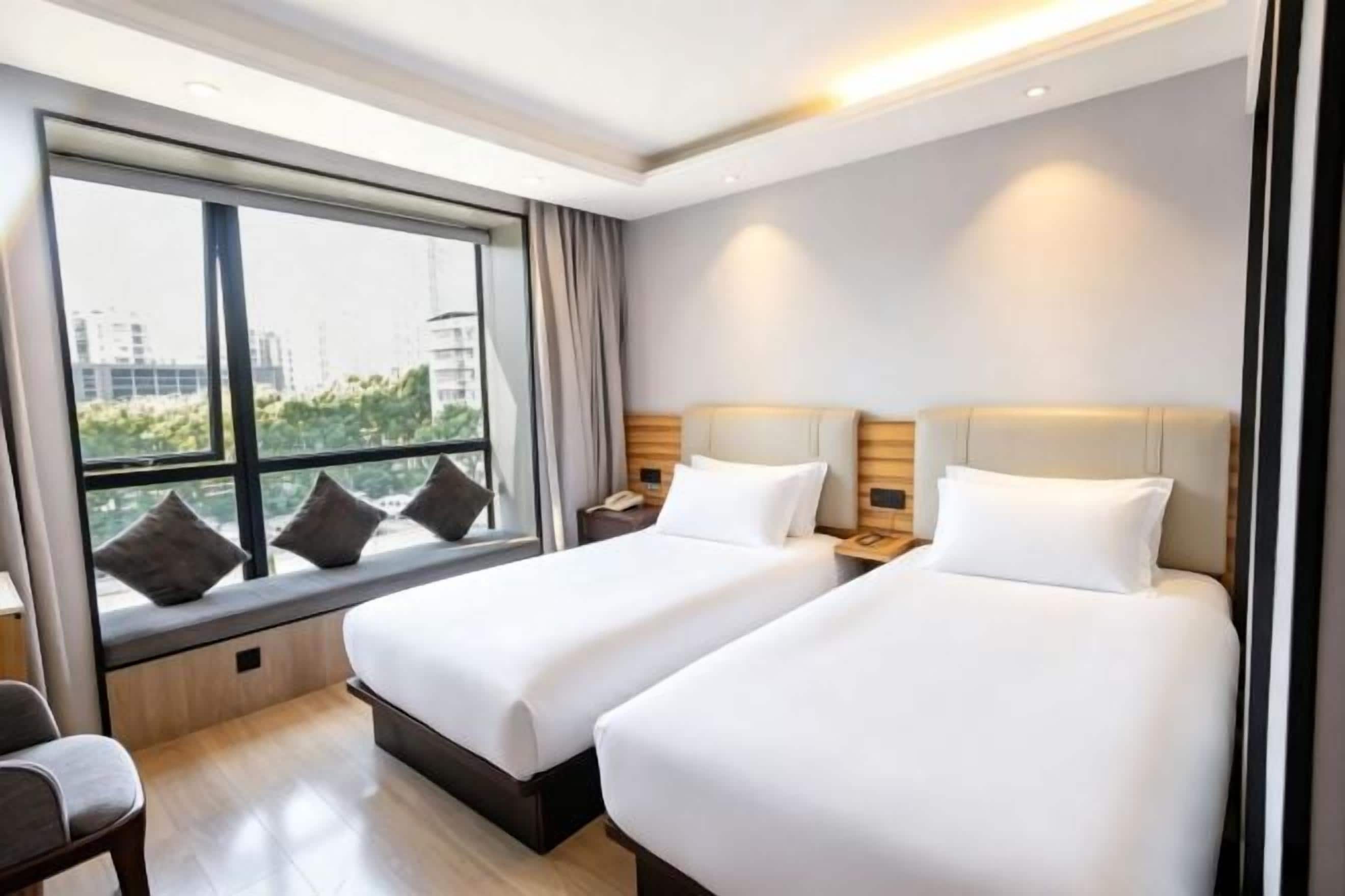 Quarto de hotel com duas camas, janela com vista para a cidade, uma escrivaninha e uma cadeira.
