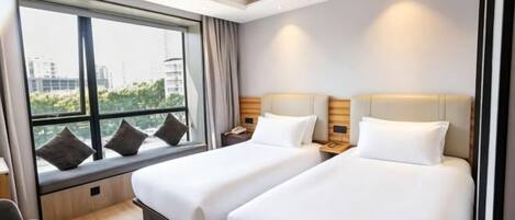 Quarto de hotel com duas camas, janela com vista para a cidade, uma escrivaninha e uma cadeira.