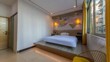 Quarto de hotel moderno com cama, mesas de cabeceira, um pequeno espaço de estar e vista pela janela.