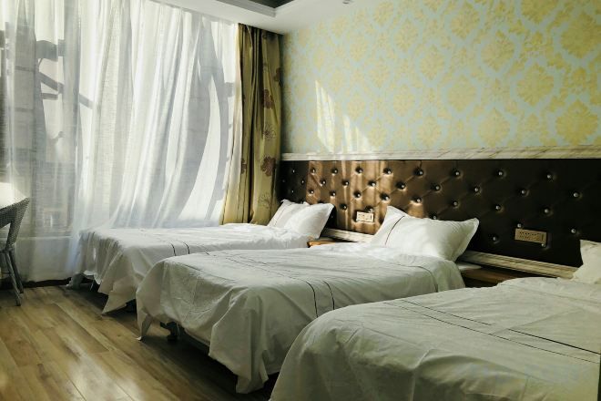 Quarto de hotel com duas camas, piso de madeira, janela grande com cortinas leves e parede estampada.